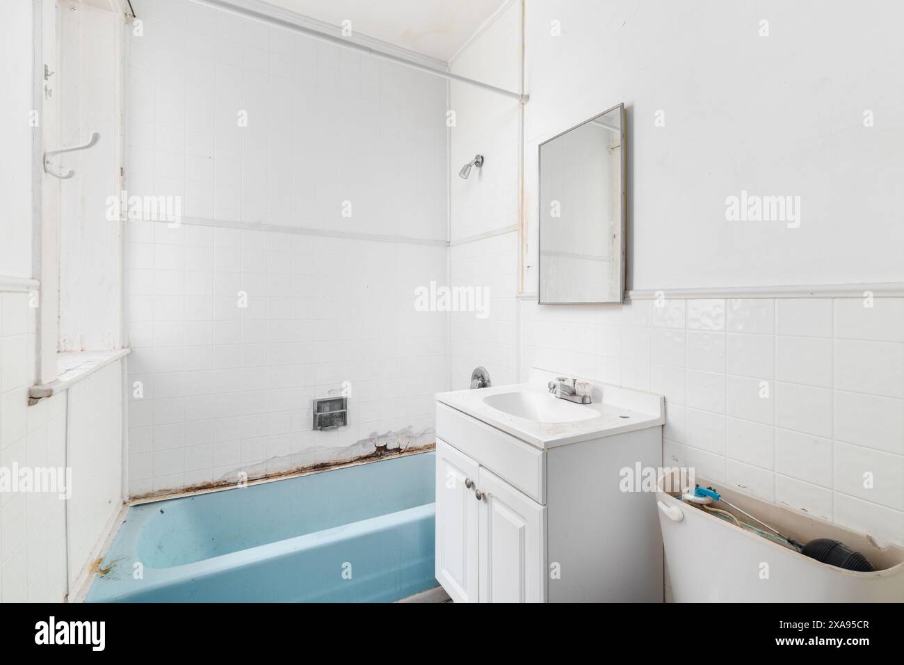 A bathroom with water damage and falling apart with white square tiles ...