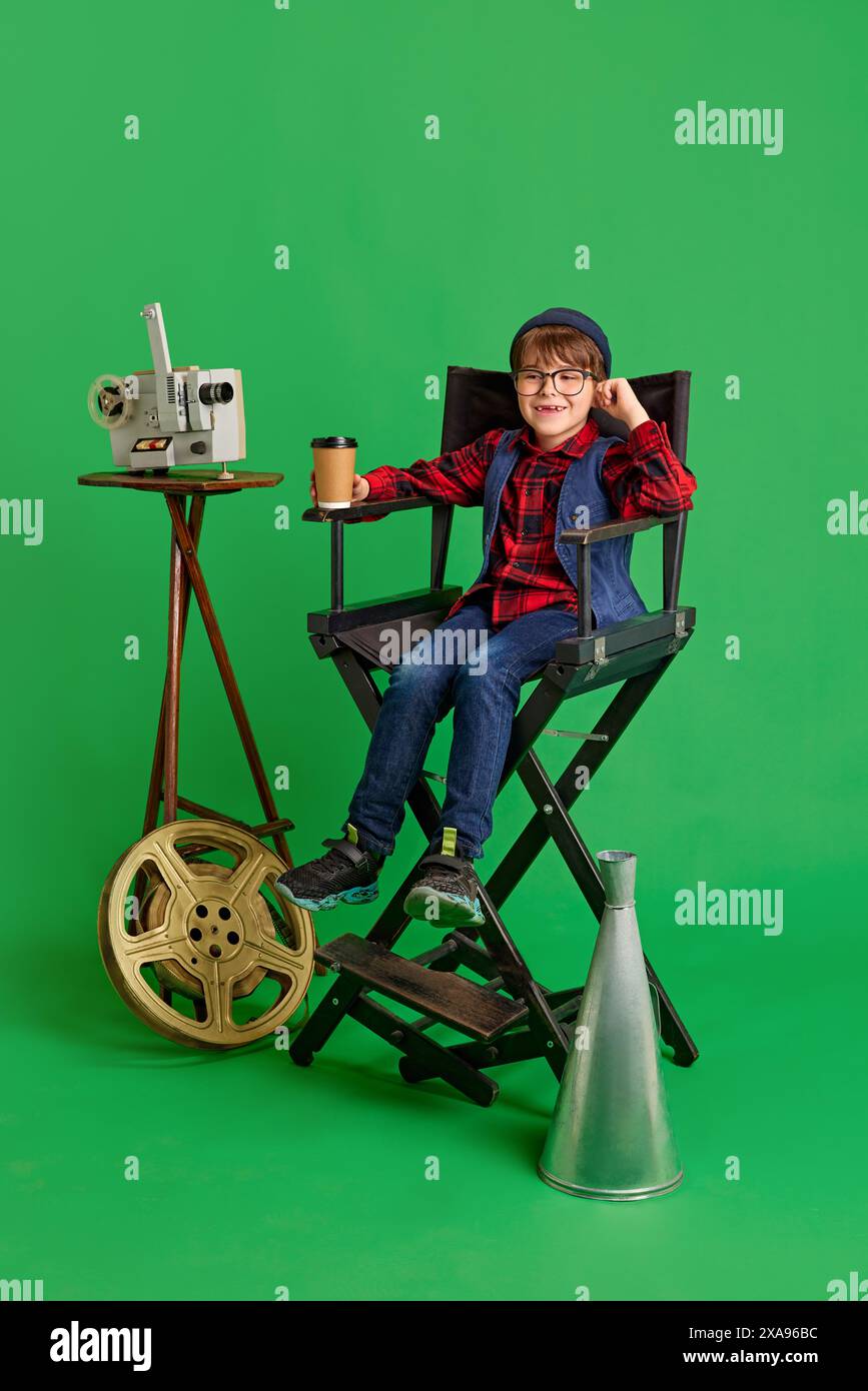 Child dressed as film director sits in director's chair, holding coffee ...