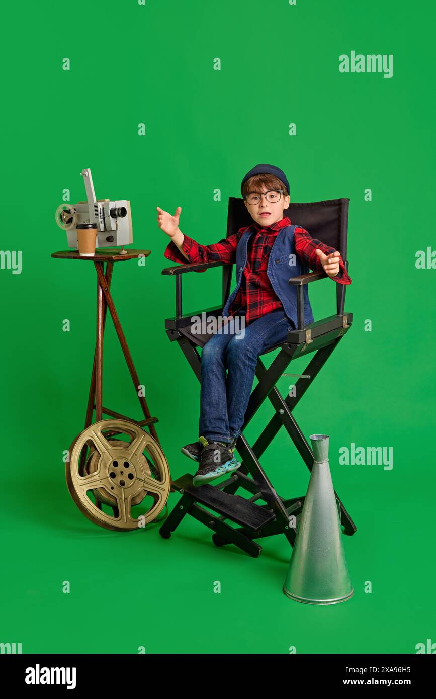 Little boy in plaid shirt and glasses, sitting in director's chair with ...