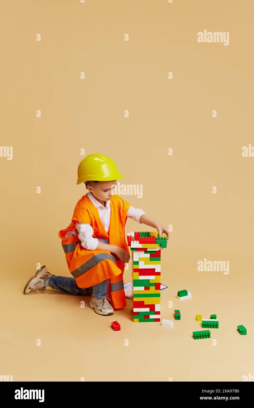 Little boy in builder's attire inspecting colorful block tower ...