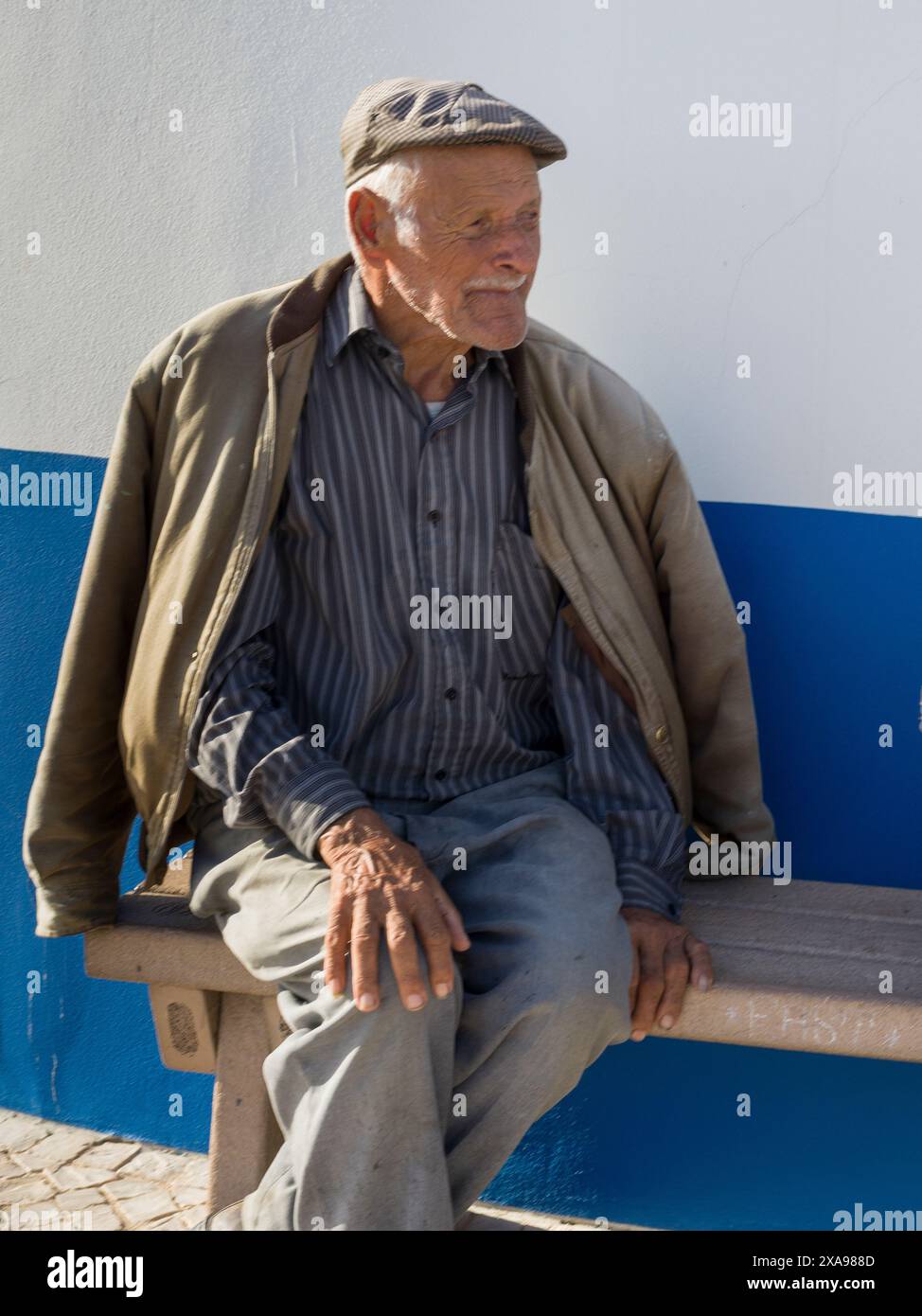 Senior elderly man sitting on a bench in a village in Portuga that lies ...