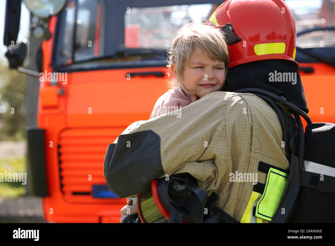 Firefighter in uniform holding rescued little girl near fire truck ...