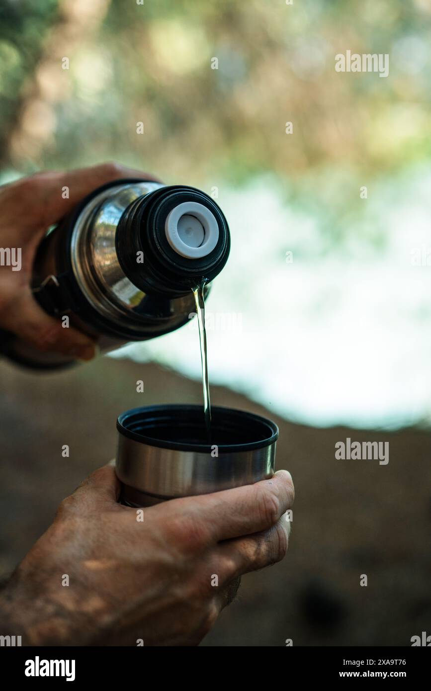 A man pours water into a metal cup by a river Stock Photo - Alamy