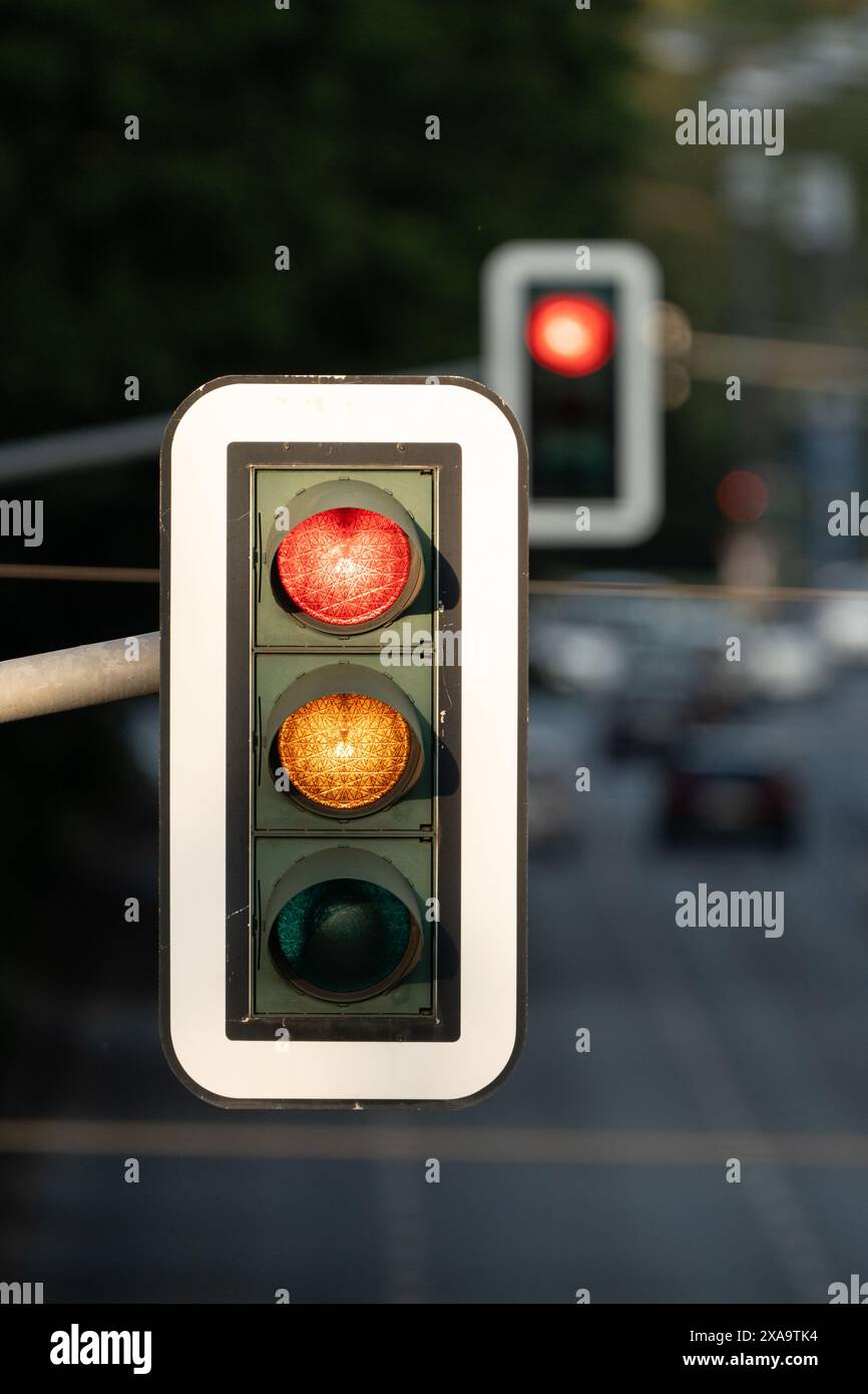 A close up of a sunlit red traffic light with the dark city in the ...