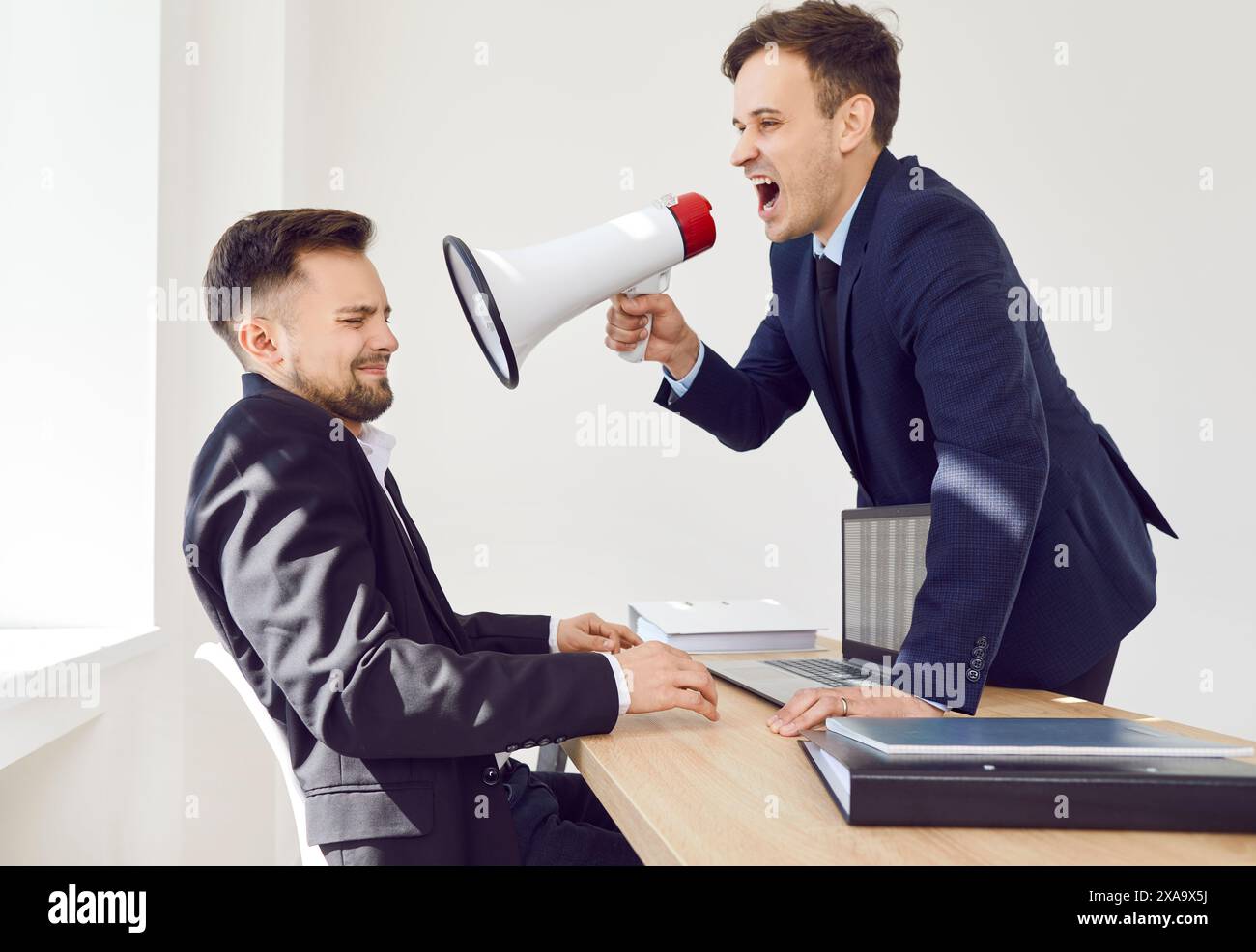 Angry boss shouting with megaphone on a employee working at the desk on ...