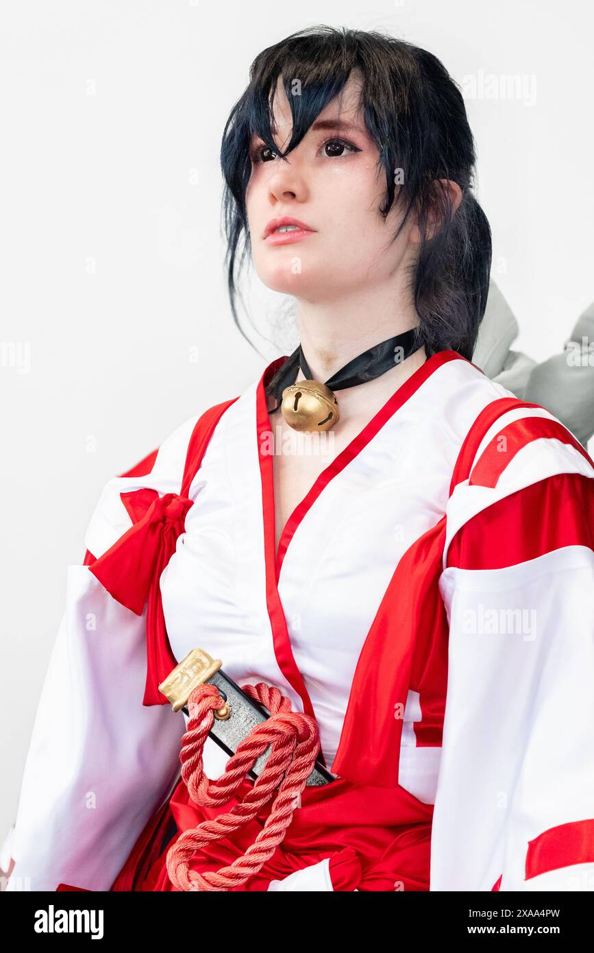 A female cosplayer in a white and red outfit with black hair and a bell ...