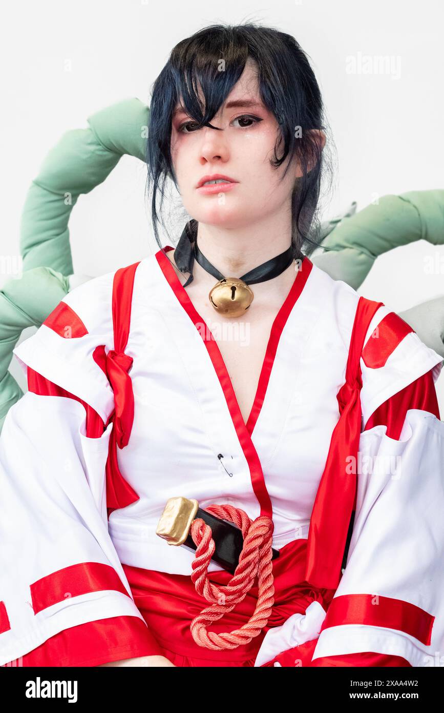 A female cosplayer in a white and red outfit with black hair and a bell ...