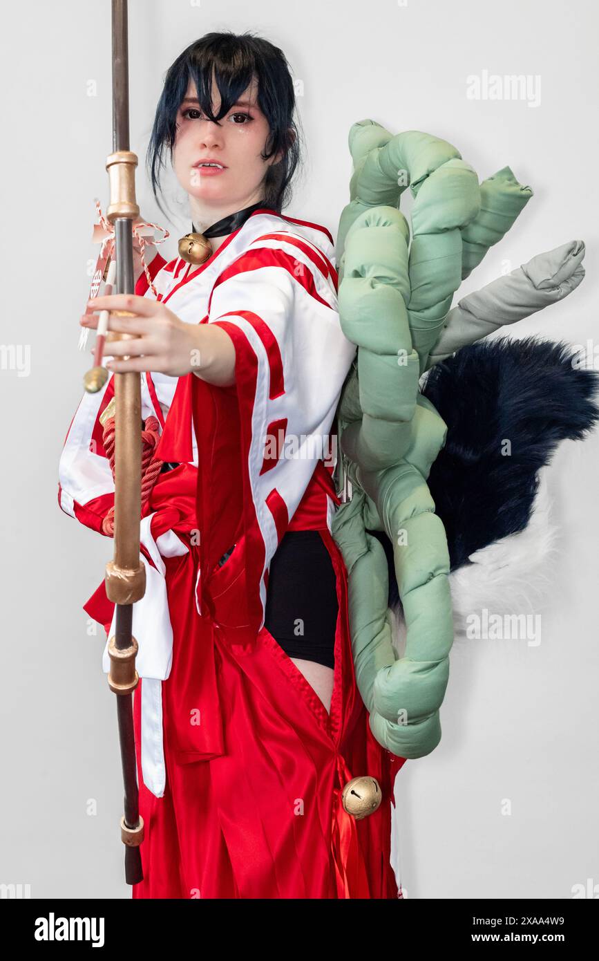 A female cosplayer in a white and red outfit and a bell around her neck ...