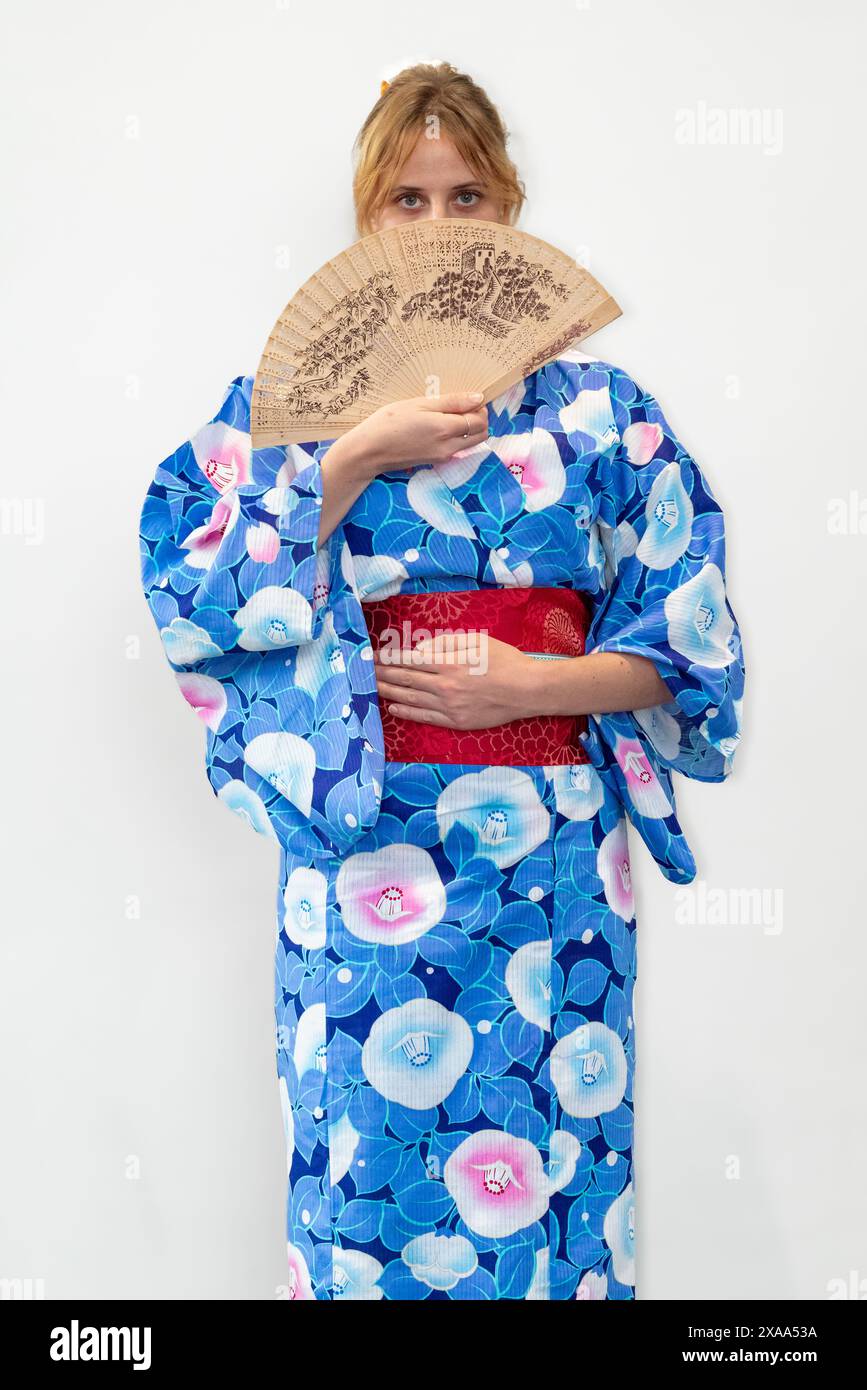A female cosplayer in a blue kimono with a red sash holding a wooden ...