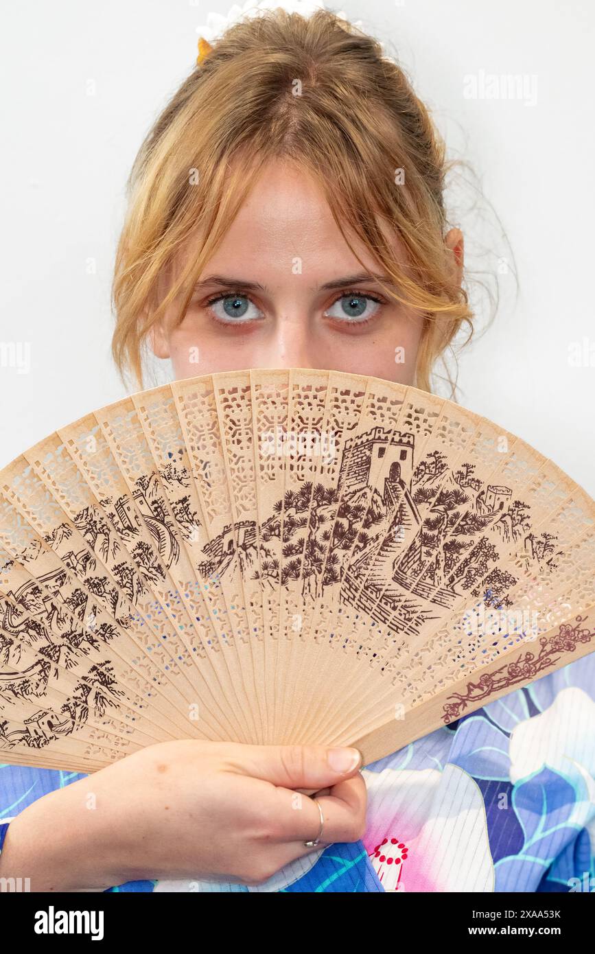 A female cosplayer in a blue kimono with a red sash holding a wooden ...