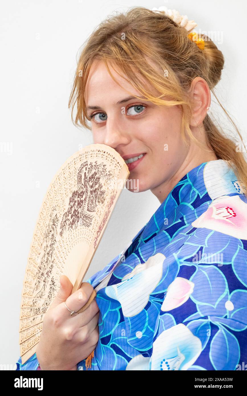 A female cosplayer in a blue kimono with a red sash holding a wooden ...