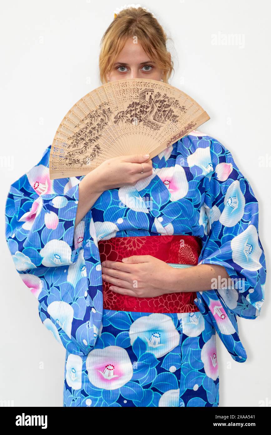 A female cosplayer in a blue kimono with a red sash holding a wooden ...