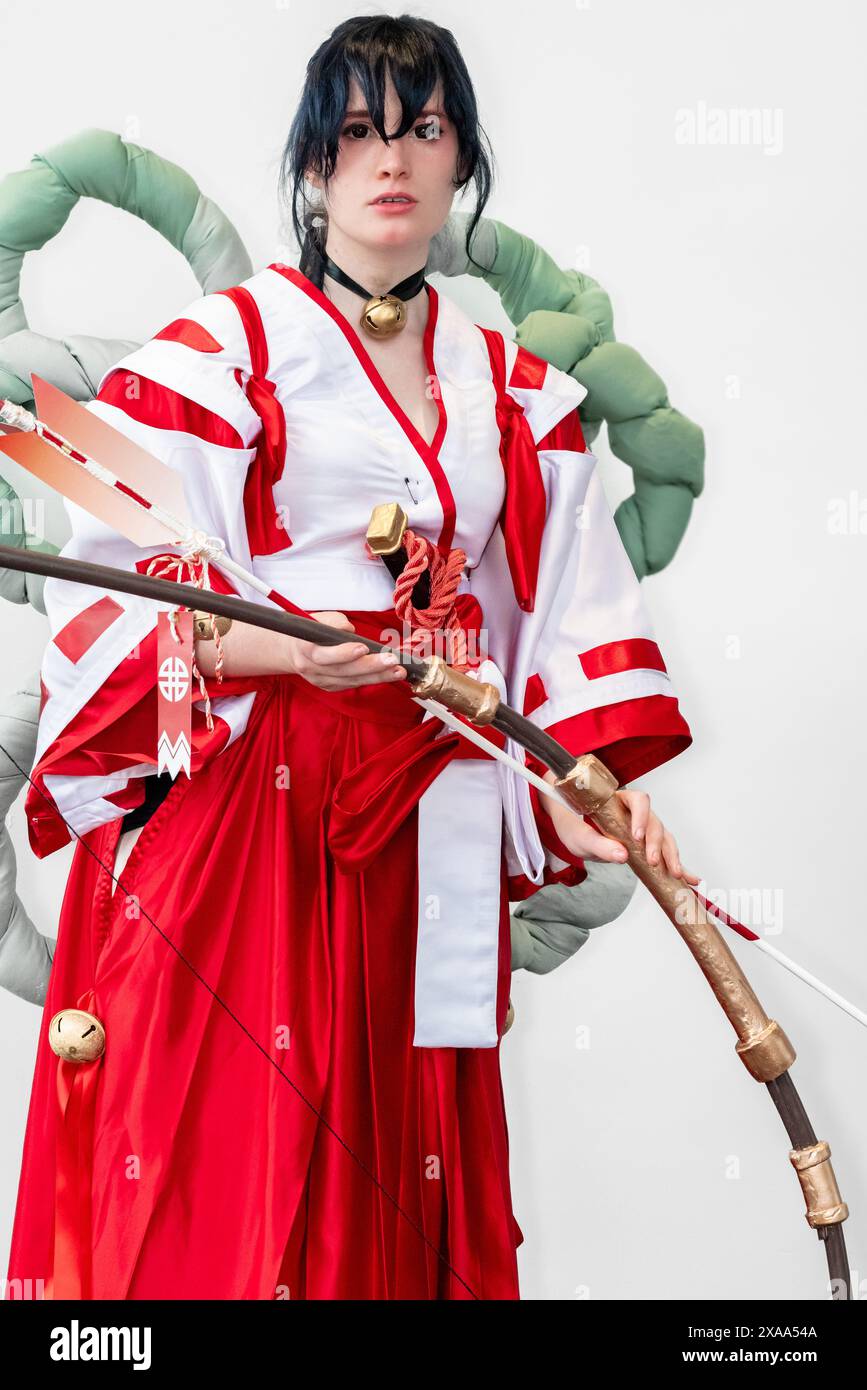 A female cosplayer in a white and red outfit and a bell around her neck ...