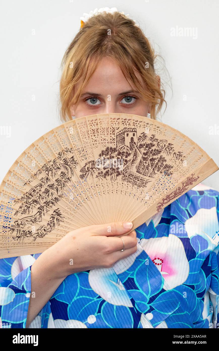 A female cosplayer in a blue kimono with a red sash holding a wooden ...