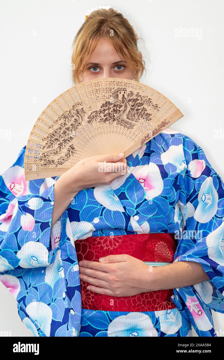 A female cosplayer in a blue kimono with a red sash holding a wooden ...