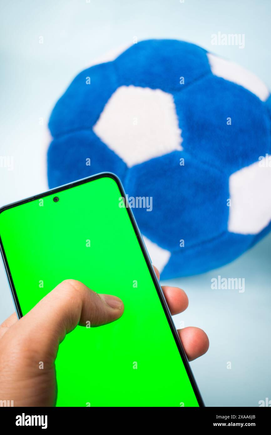 A hand holding a smartphone with a green screen against a plush soccer ...