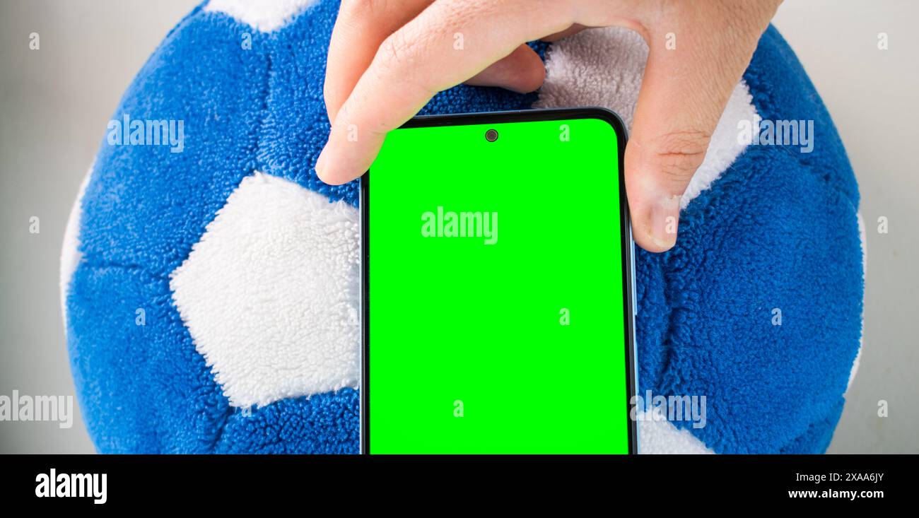 A hand holding a smartphone with a green screen positioned on a plush ...