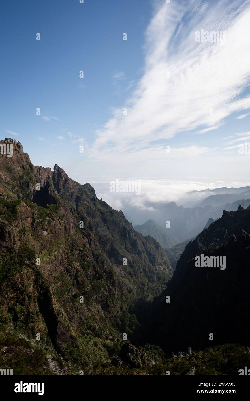 A rugged mountain peak rises above sharp cliffs amidst clouds Stock ...