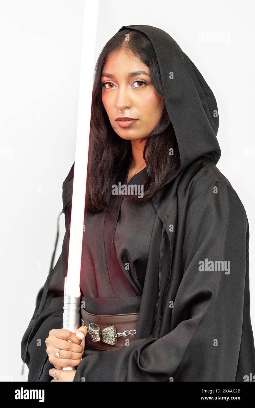 A woman in robes wields a light sword against a white wall backdrop ...