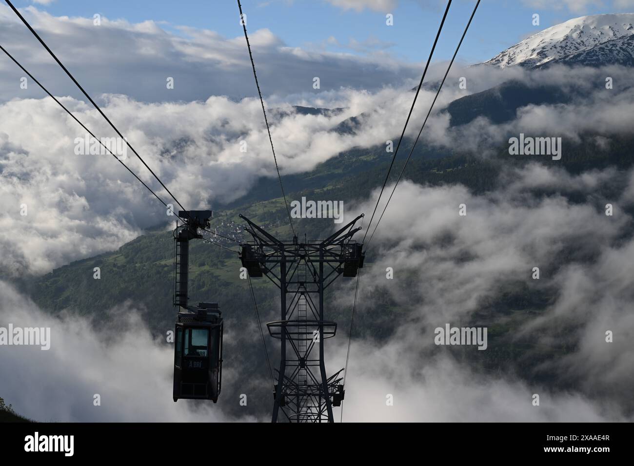 A Gondola lift descending mountain with view of clouds below Stock ...