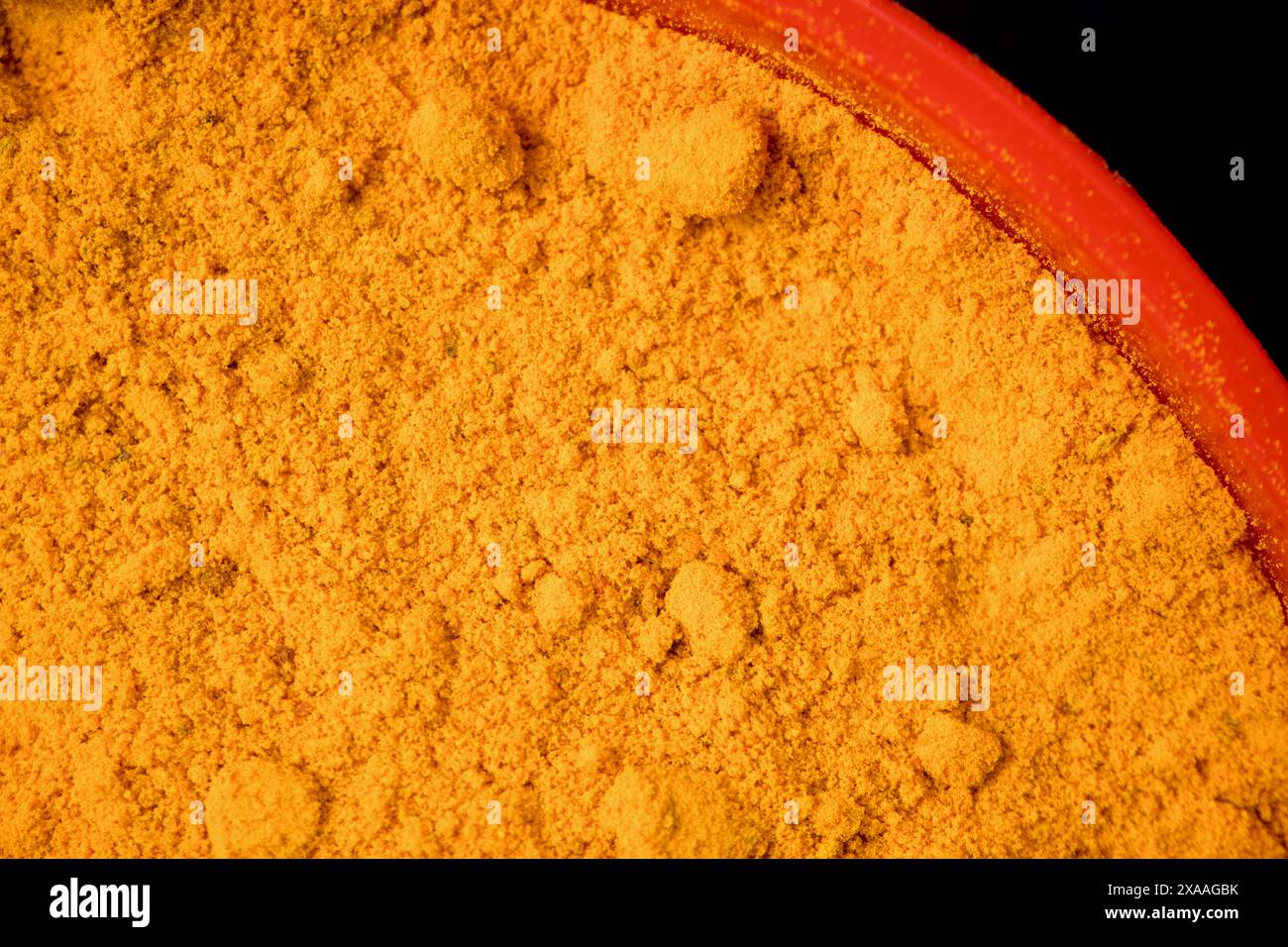 A mound of turmeric powder in a red bowl, captured in a close-up shot ...