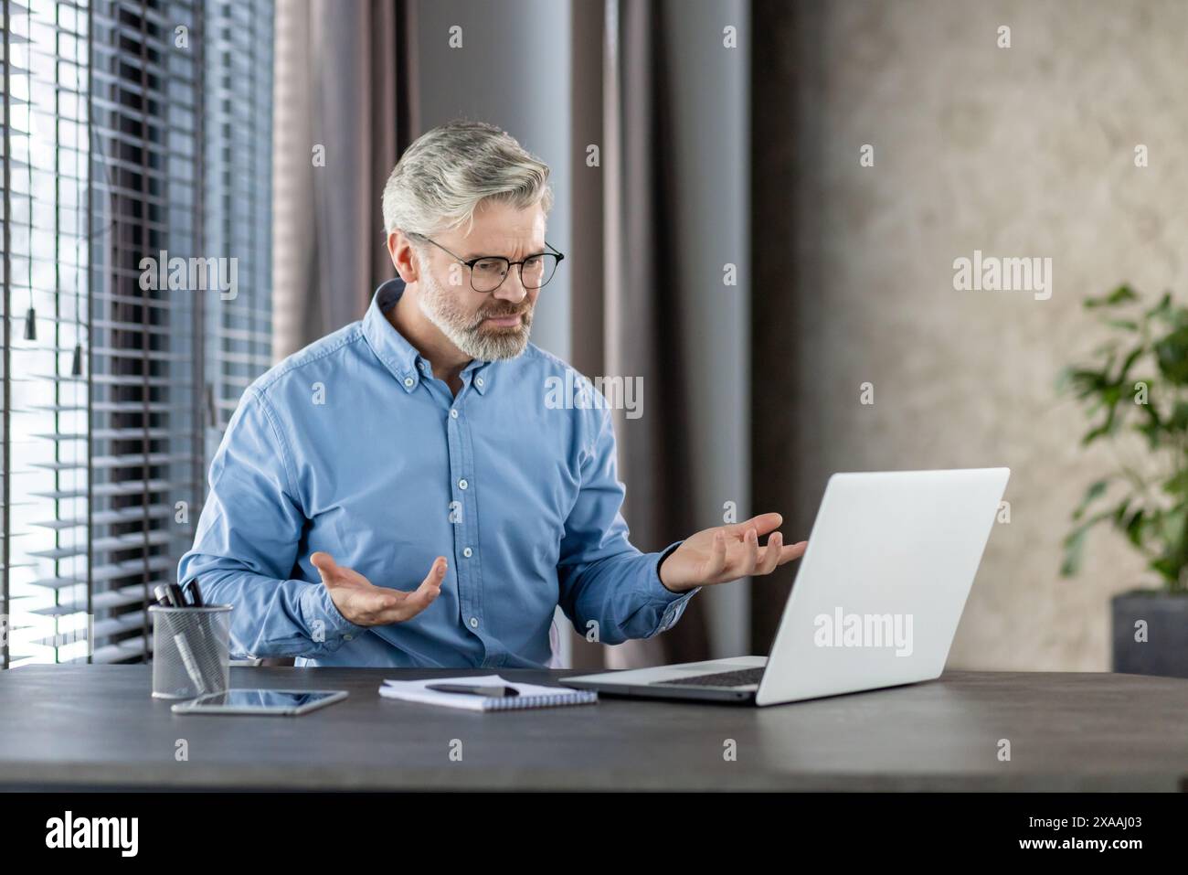Senior businessman expressing frustration during a video call on a ...