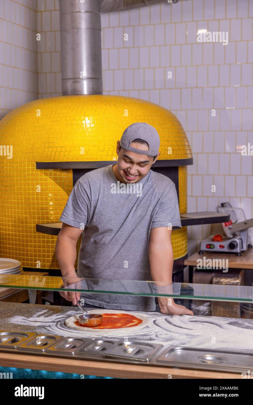 Chef pours tomato sauce over the rolled dough. Chef hand is spreading ...