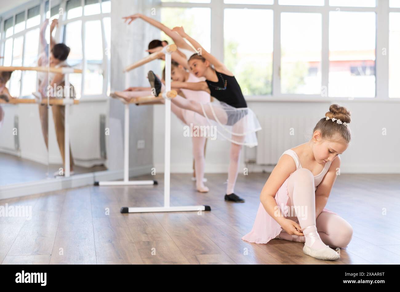 Girl sits on floor and adjusts her shoes, ties ribbons around her shin ...