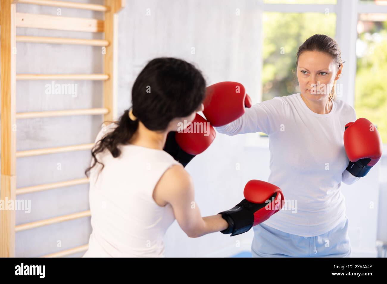 Focused woman practicing boxing punches in sparring during group self ...