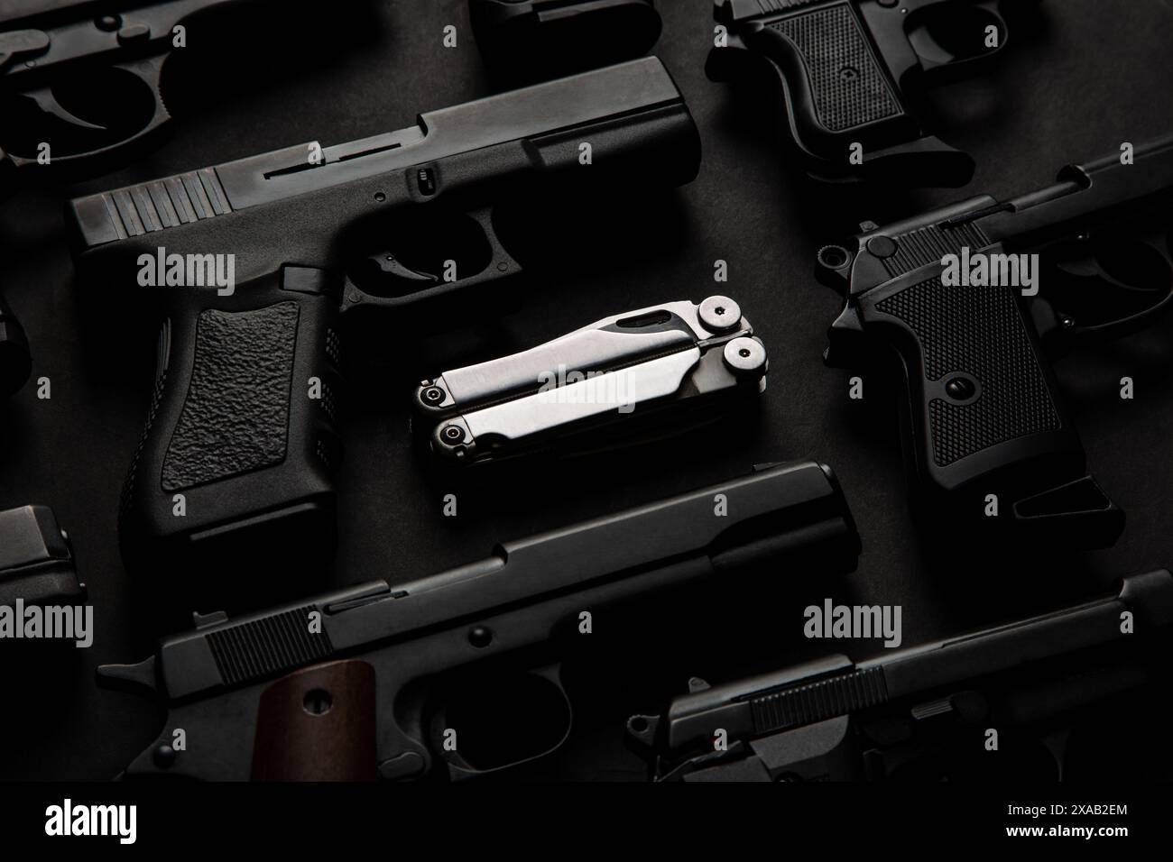 Silver multi-tool among various semi-automatic pistols. Dark background ...