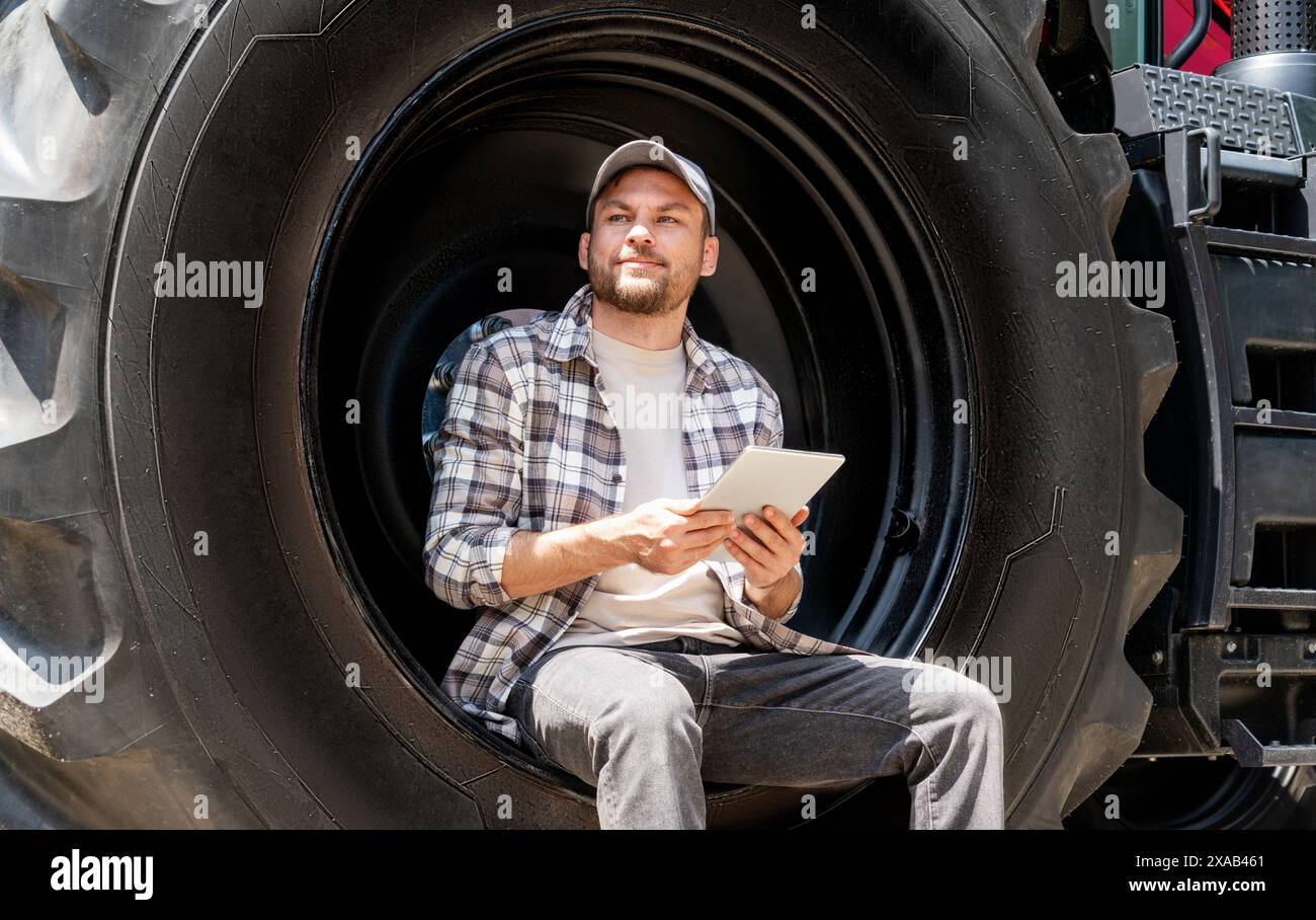 Man farmer sits on the big wheel of agricultural tractor and using his ...