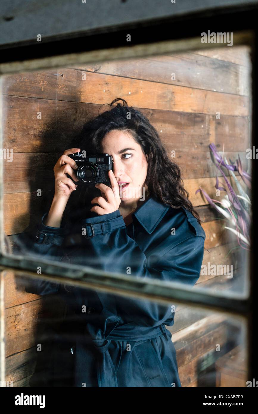 Young woman in trenchcoat taking pictures with an analogue camera ...