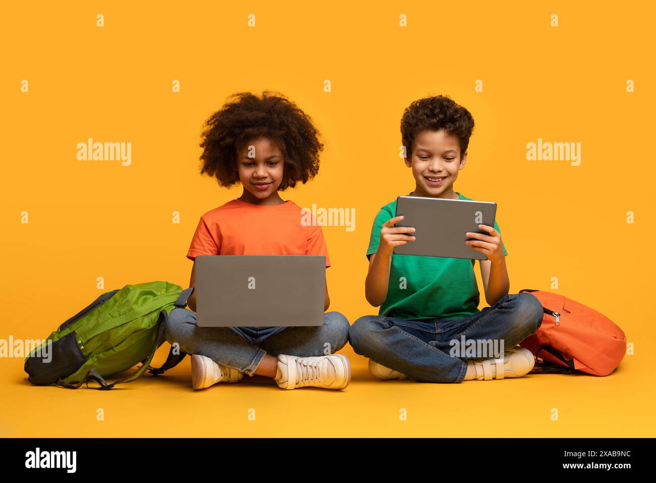 Two Children Using Technology While Sitting on Yellow Background Stock ...