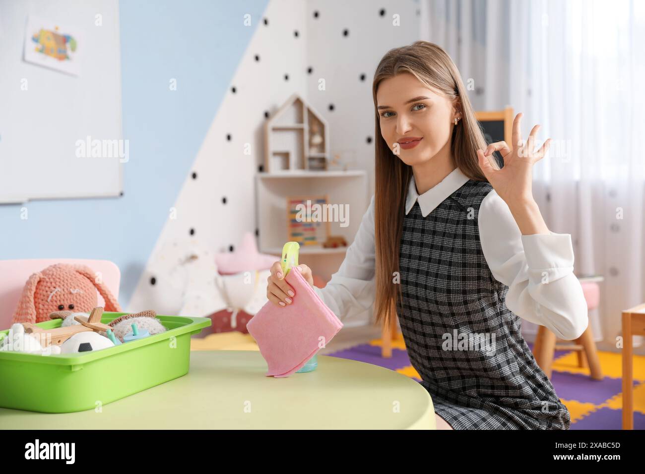 Female nursery teacher with rag and detergent showing OK in ...