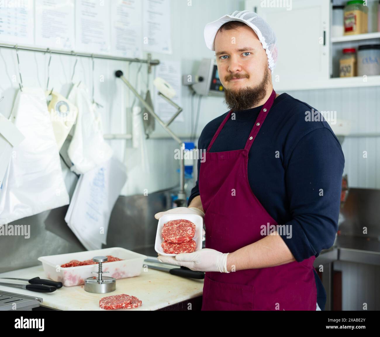 Bearded butcher offering ground veal burger patties in plastic tray ...