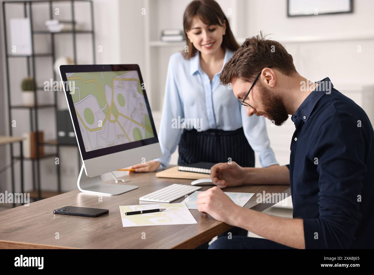 Cartographers working with cadastral map on computer at table in office ...