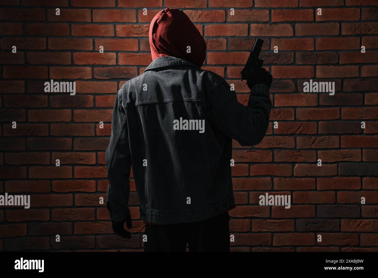 Thief in hoodie with gun against red brick wall, back view Stock Photo ...