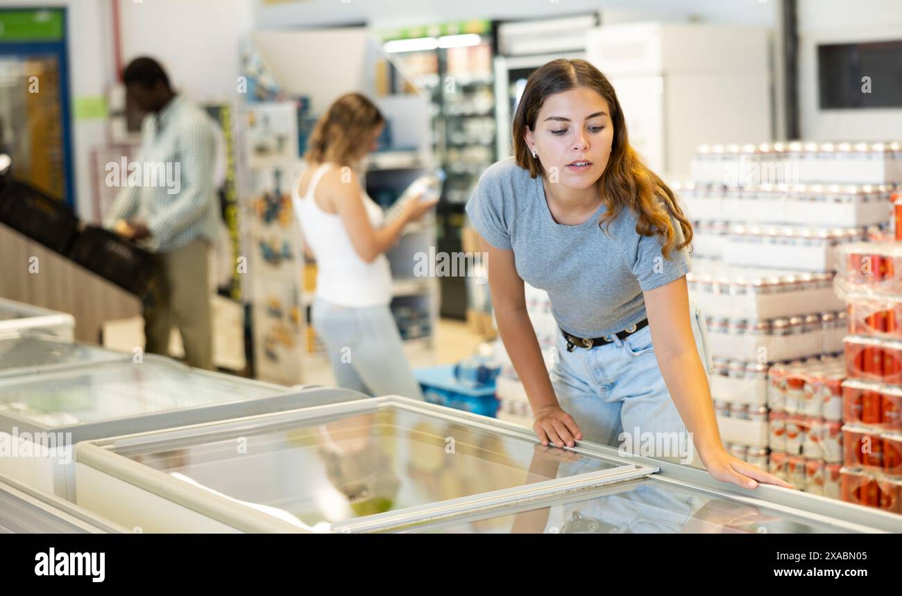 Female shopper carefully chooses frozen food in grocery supermarket ...