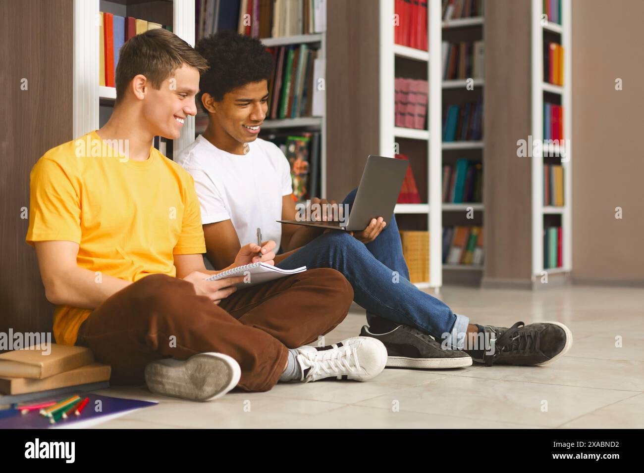Two young guys studying on floor in library Stock Photo - Alamy
