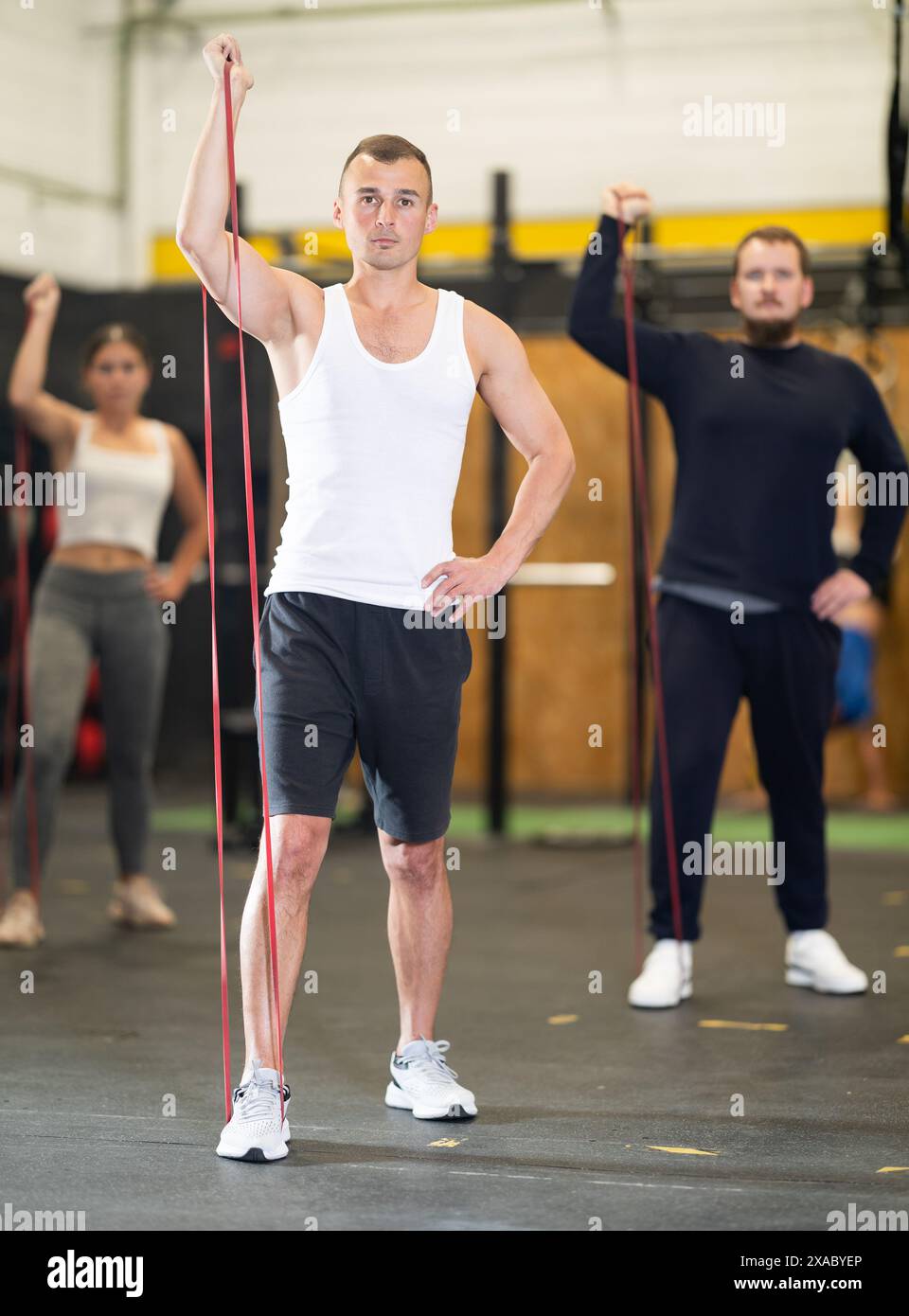 Sporty man doing exercises with elastic loop band during group workout ...
