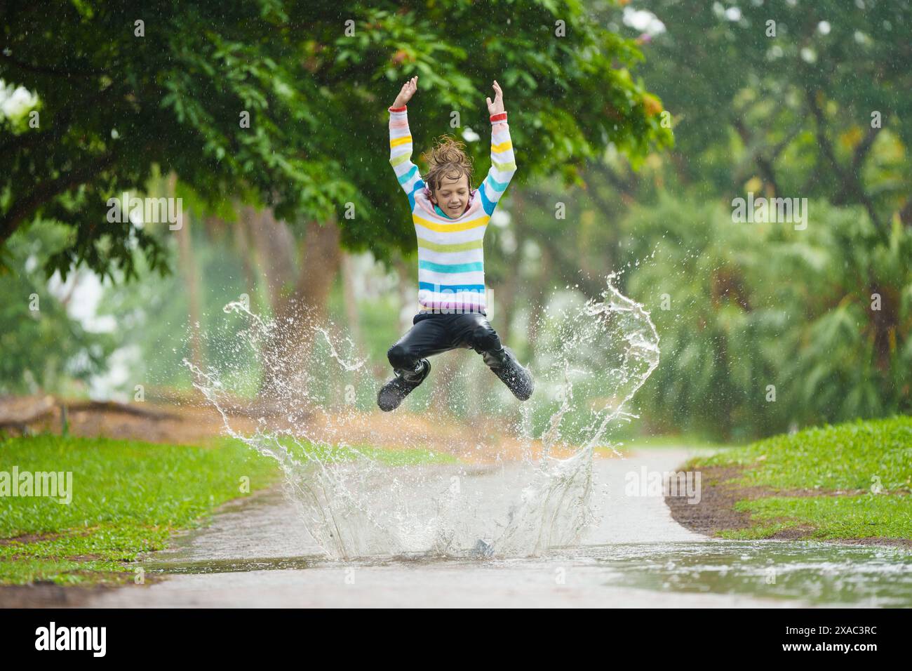 Child playing in autumn rain. Kid jumping in muddy puddle in beautiful park. Little boy with ...