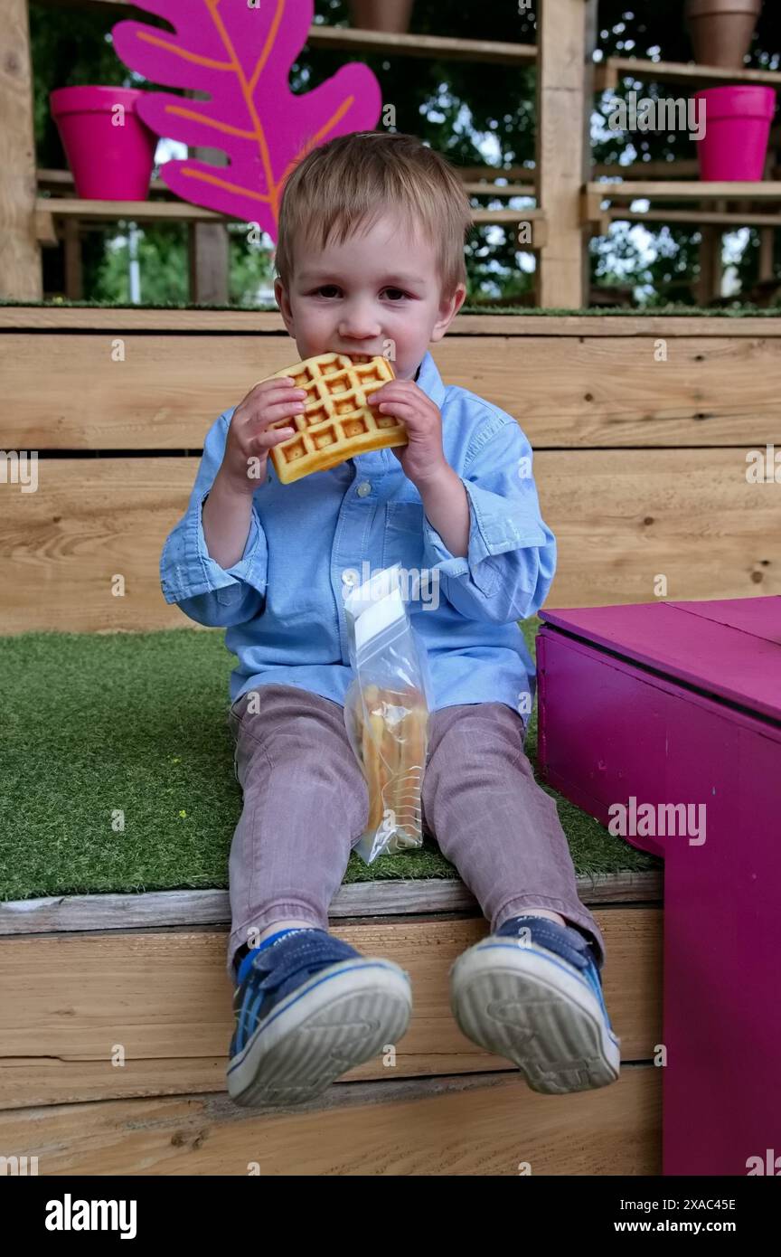 Little toddler sitting on the bench and eating cookies Stock Photo - Alamy