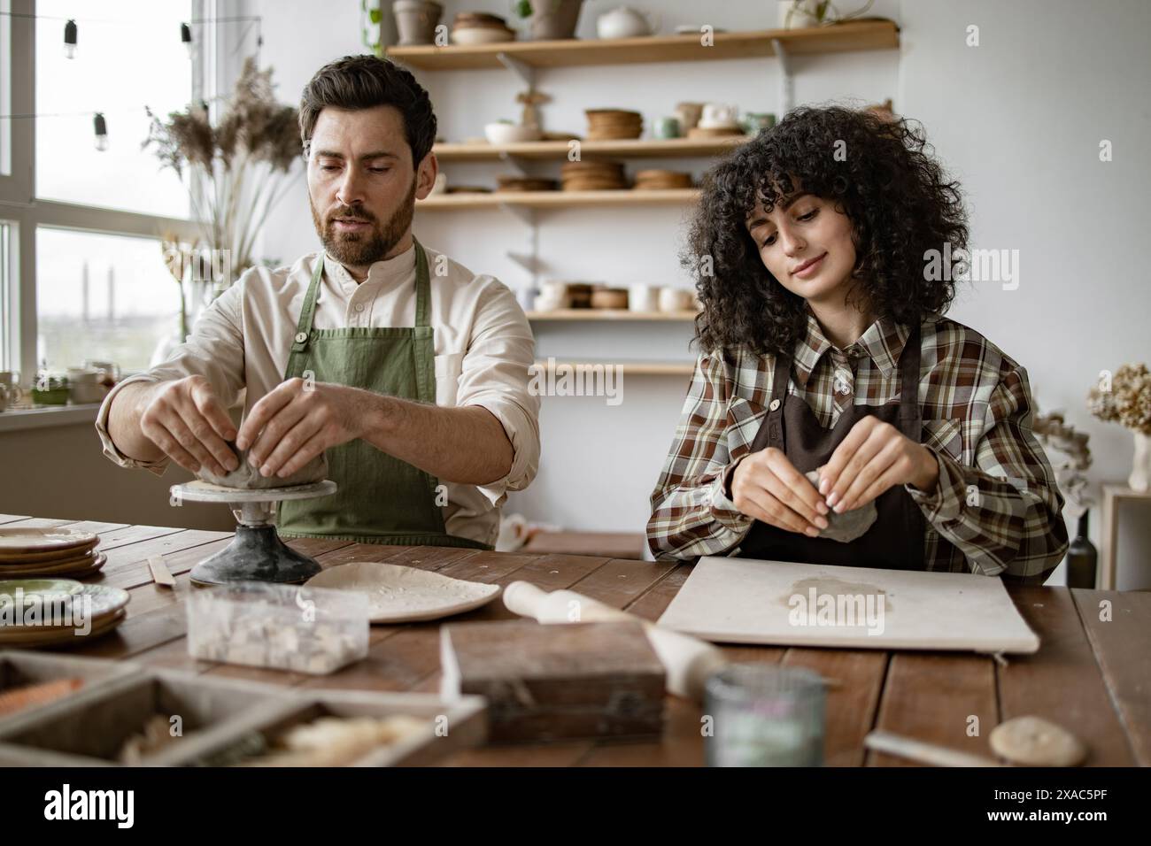 Bearded mature man and woman engaged in sculpting clay in a pottery ...