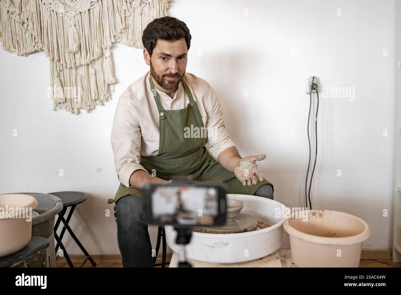 Mature man creating pottery on wheel and recording video blog. Hands-on ...