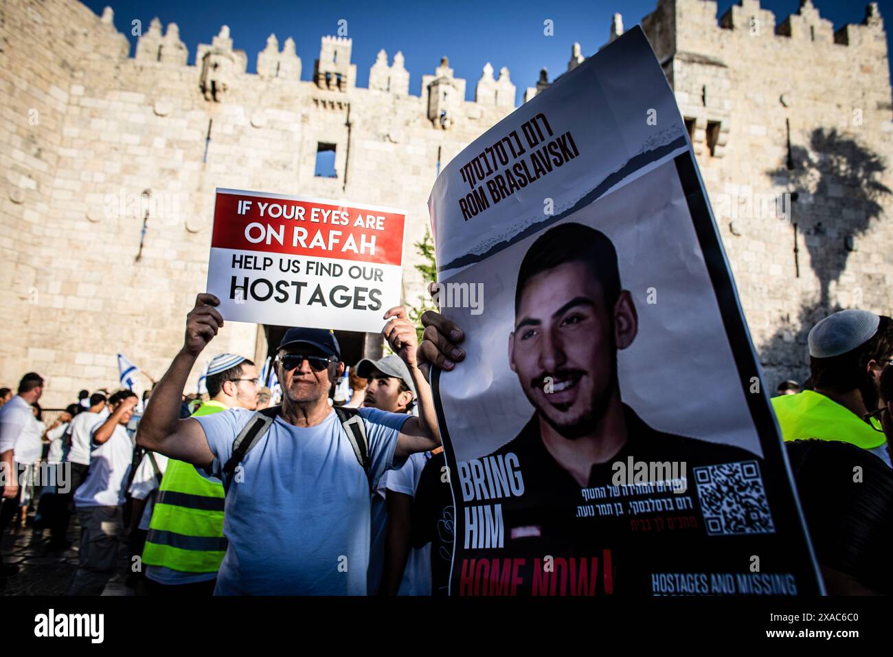 A man holds a sign next to a placard showing a photo of Rom Braslavsky ...