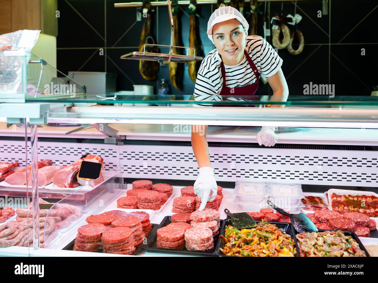 Female butcher shop vendor offering burger patties from display case ...
