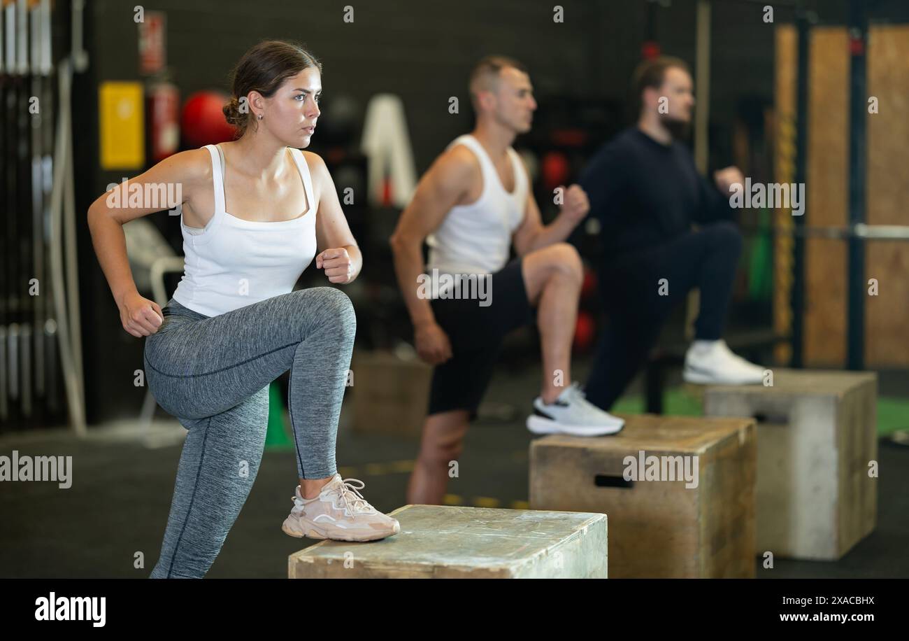 Motivated girl performing step-ups on plyo box during group workout ...