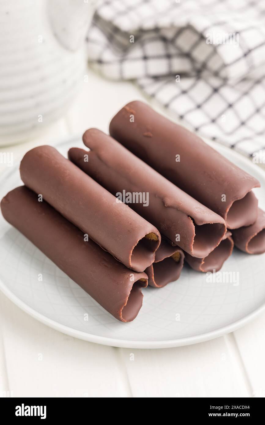 A close-up photo of chocolate-covered wafer rolls stacked on a white ...