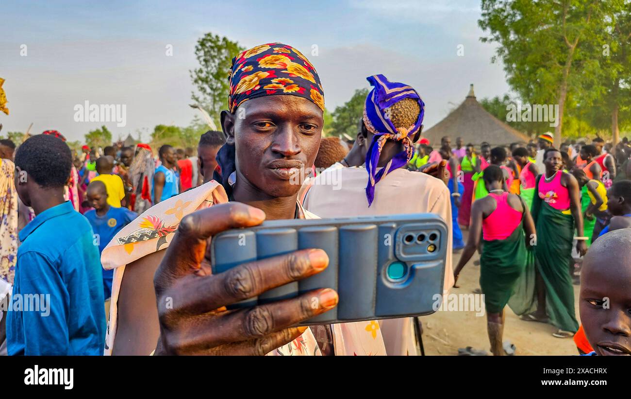 Man with cellphone taking a photo at a traditional Dinka wedding, Bor ...