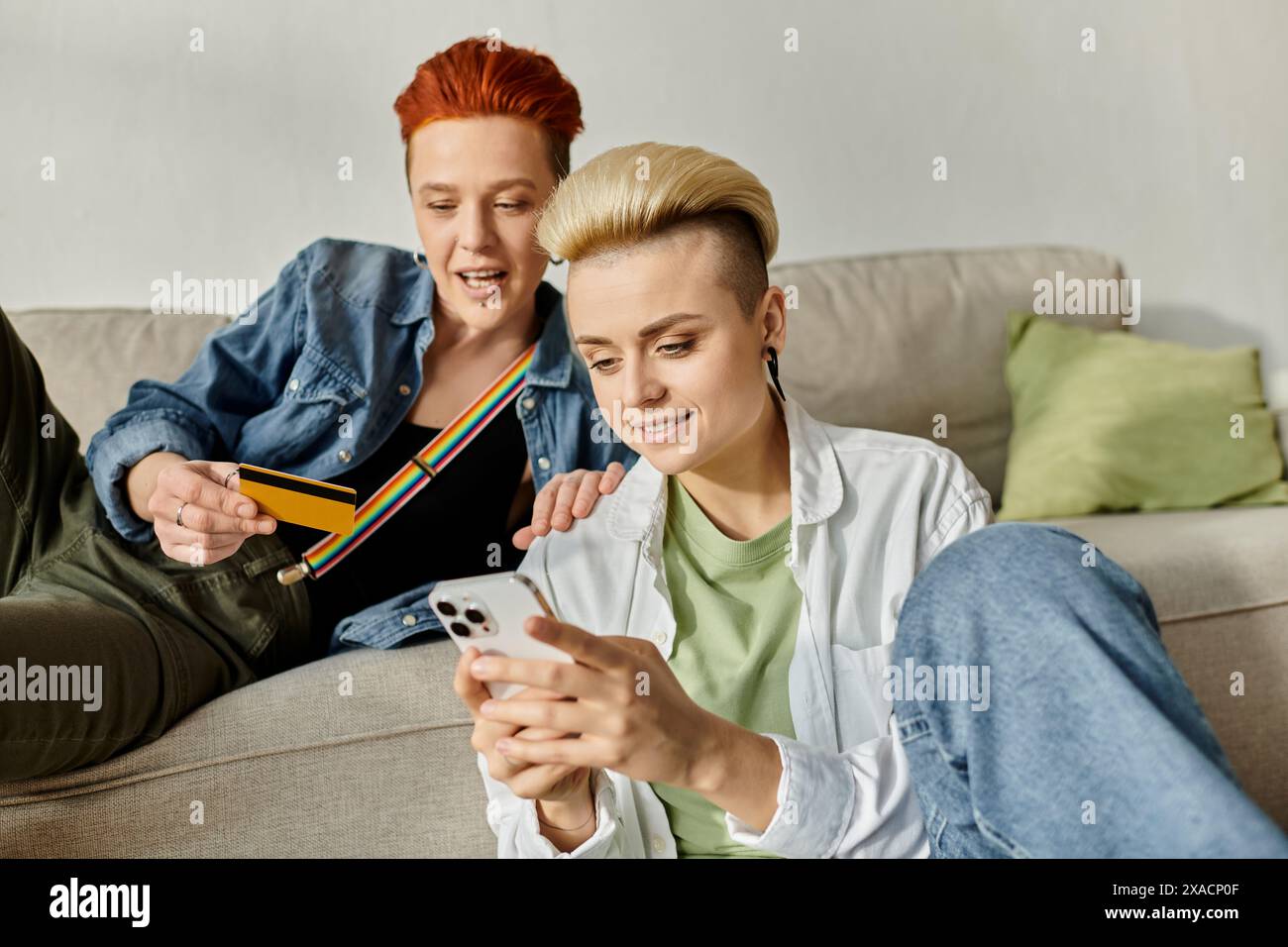 Two short-haired women sit on a couch, engrossed in a cell phones ...